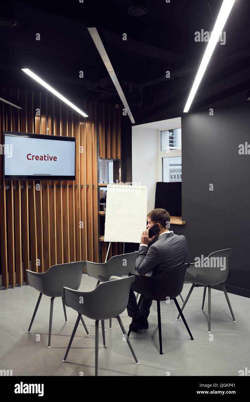 Rear view of busy young businessman in suit sitting on chair in ...