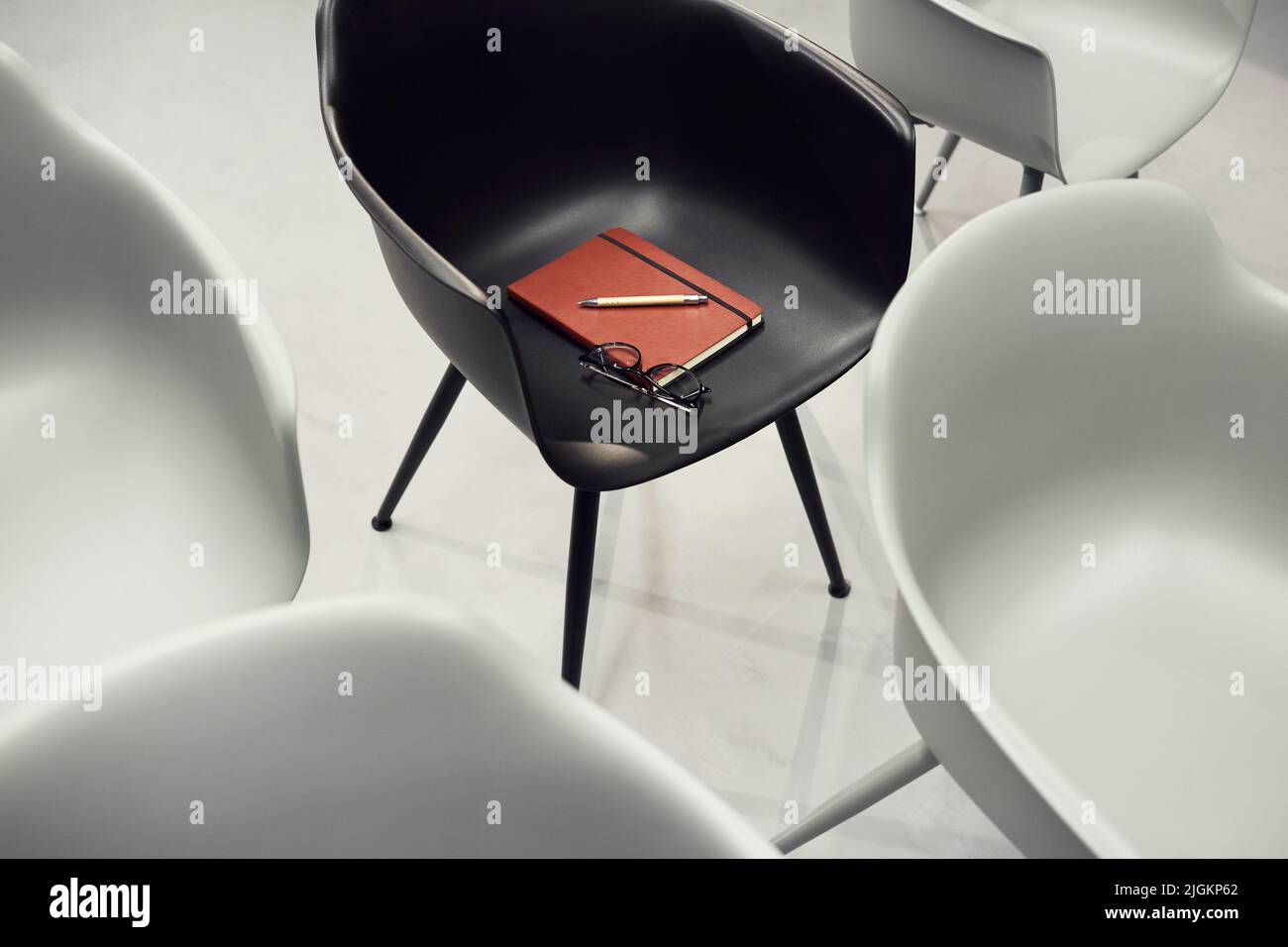 Red notepad, eyeglasses and pen on black chair among white seats in ...