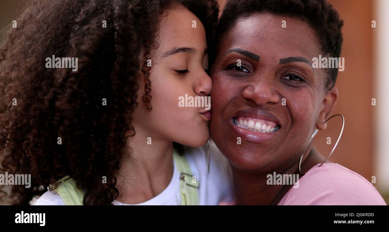 African mother and daughter together. Little girl child kissing mom on cheek, love and affection ...
