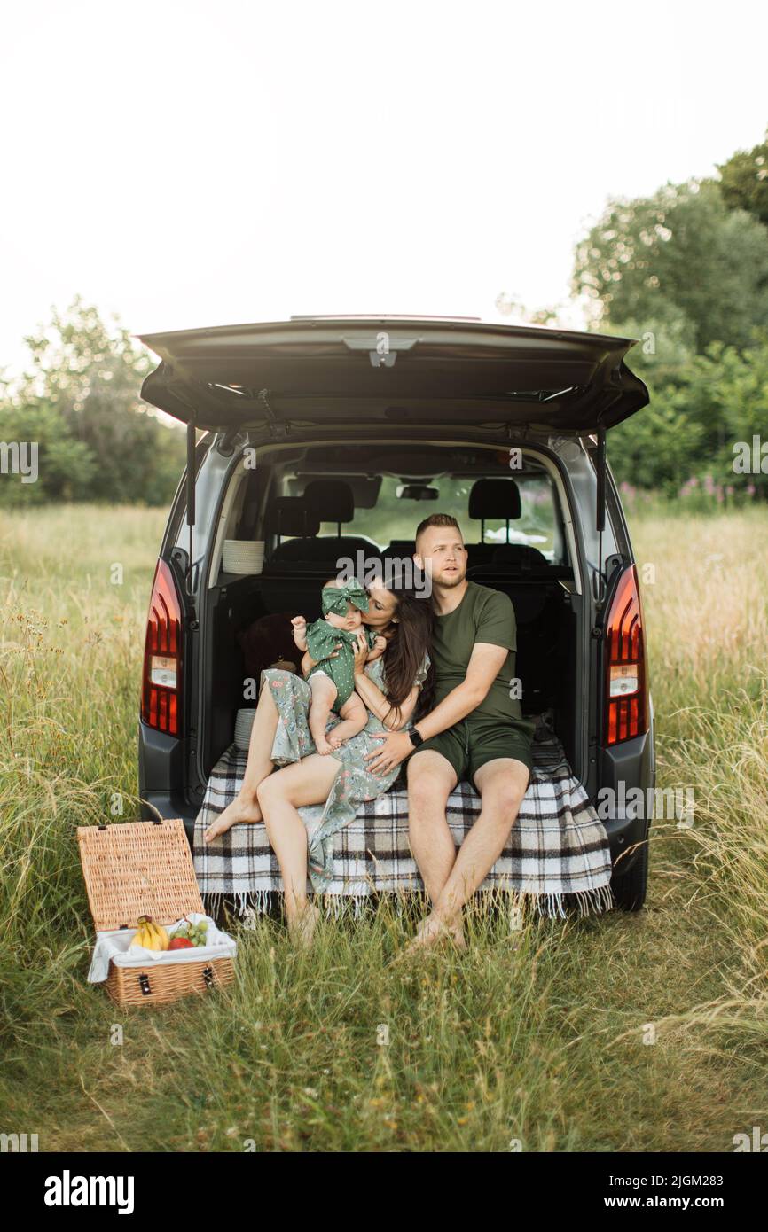 Beautiful caucasian man and woman sitting in embrace with their cute little daughter on car ...