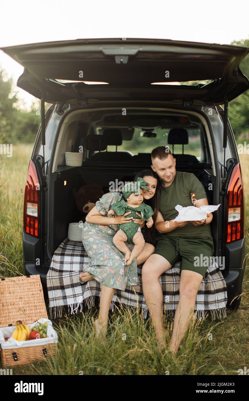 Beautiful and happy family of three sitting in car trunk with tasty ...