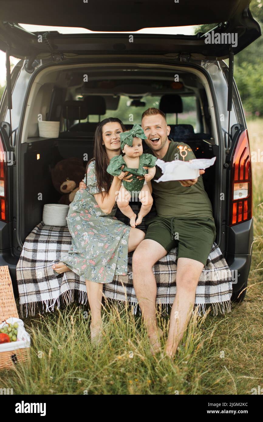 Beautiful and happy family of three sitting in car trunk with tasty ...