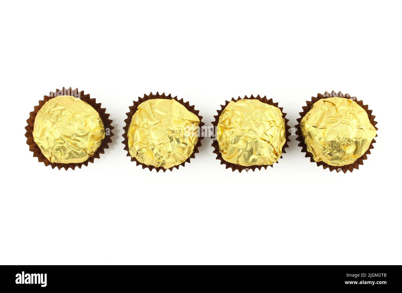 Four chocolate truffle balls wrapped in golden color foil isolated on ...
