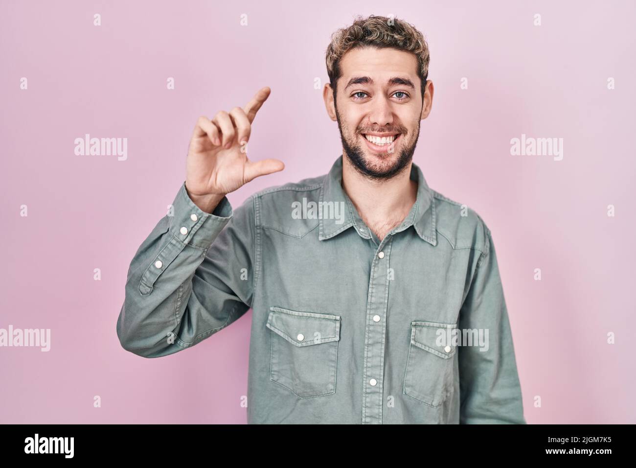 Hispanic man with beard standing over pink background smiling and ...