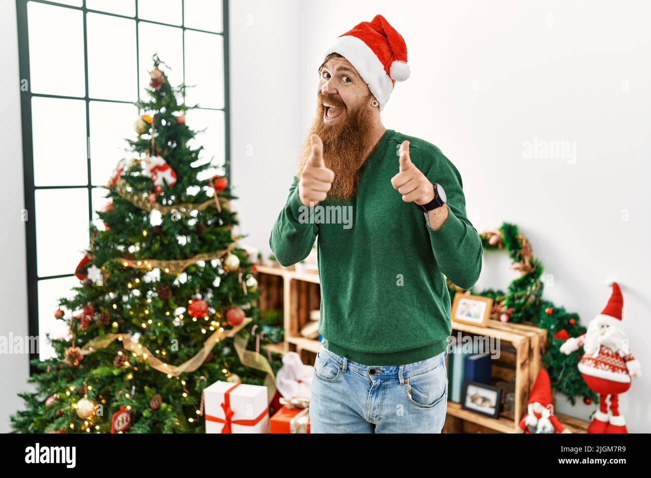 Redhead man with long beard wearing christmas hat by christmas tree ...
