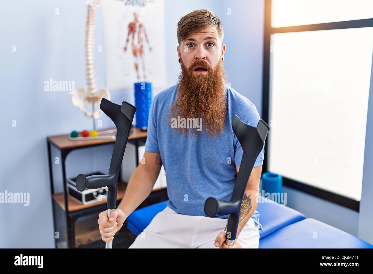 Redhead man with long beard holding crutches at rehabilitation clinic ...