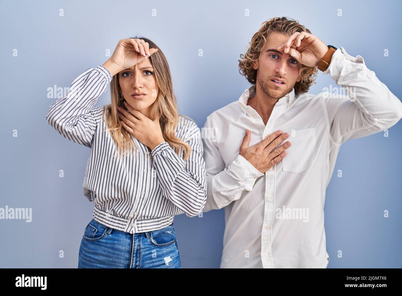 Young couple standing over blue background touching forehead for ...