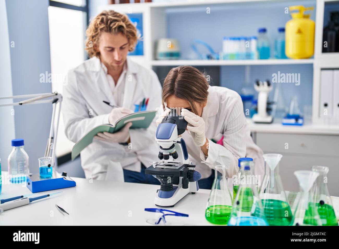Man and woman wearing scientist uniform writing on notebook using ...