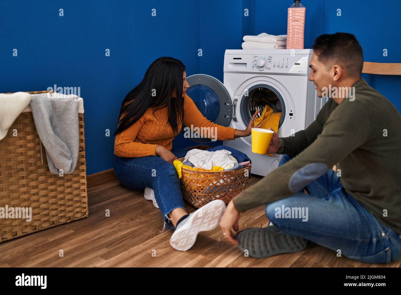 Man and woman couple washing clothes drinking coffee at laundry room Stock Photo - Alamy