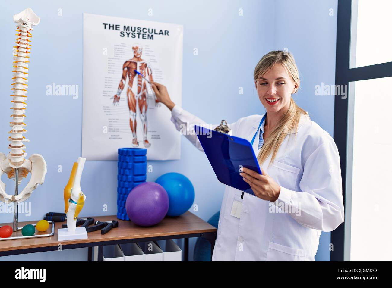 Young blonde woman wearing physiotherpist uniform pointing to anatomy ...