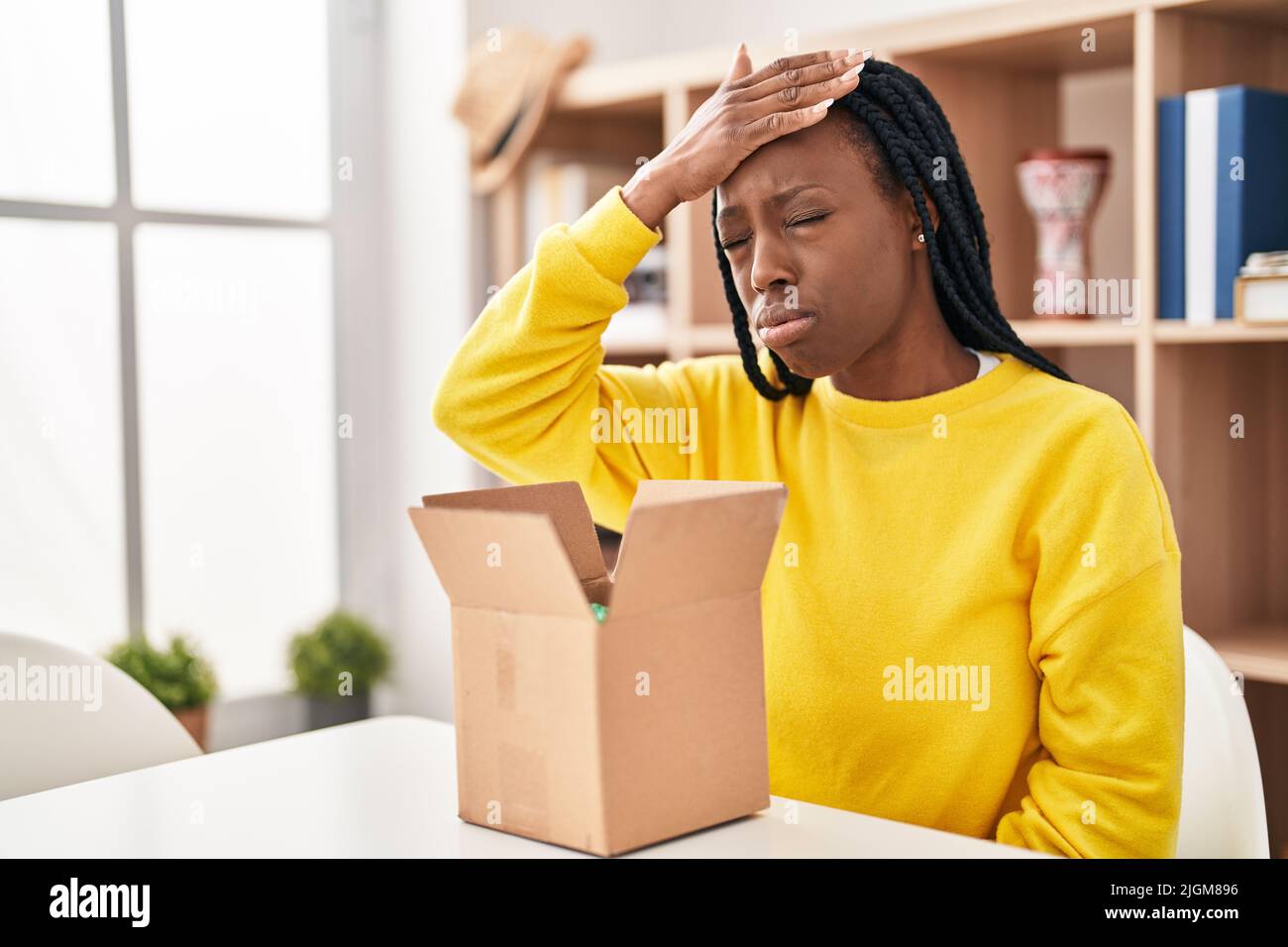 Beautiful black woman opening cardboard box surprised with hand on head ...