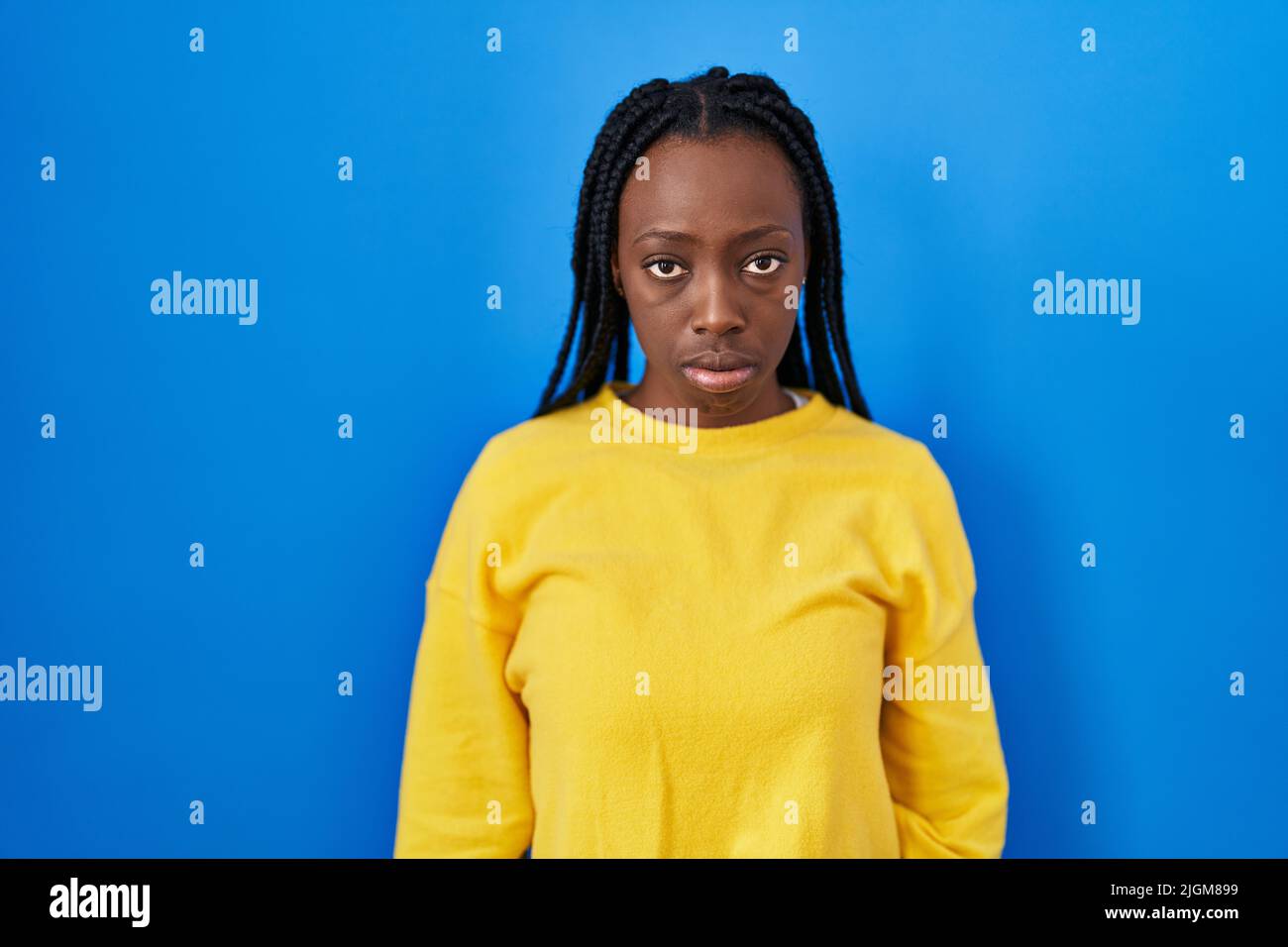Beautiful black woman standing over blue background looking sleepy and ...