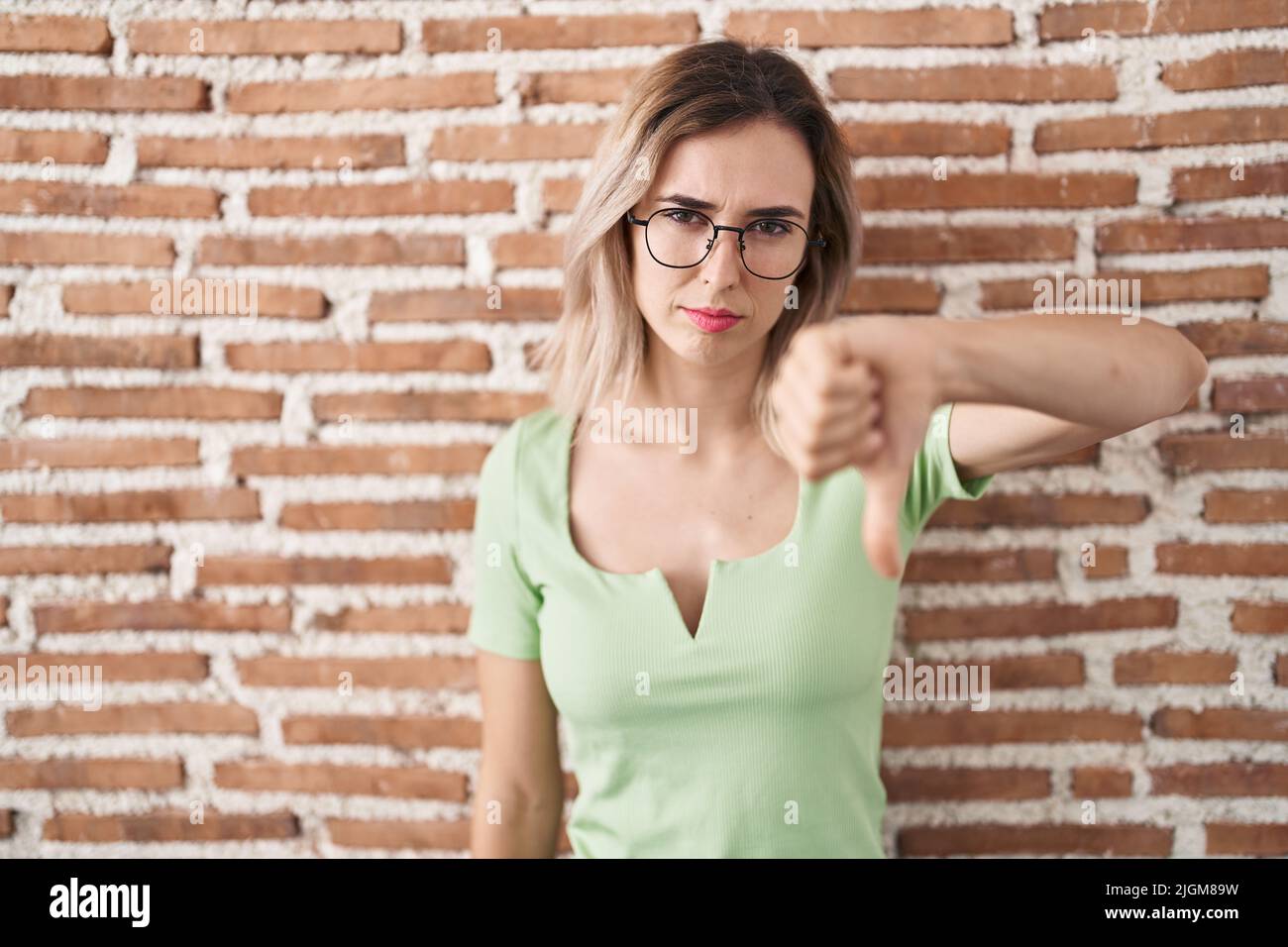 Young Beautiful Woman Standing Over Bricks Wall Looking Unhappy And