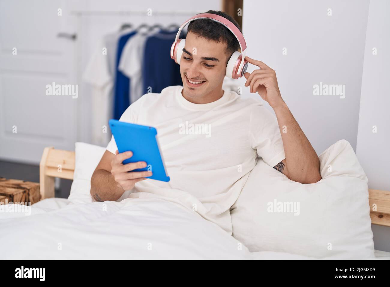Young hispanic man watching video on touchpad sitting on bed at bedroom Stock Photo - Alamy