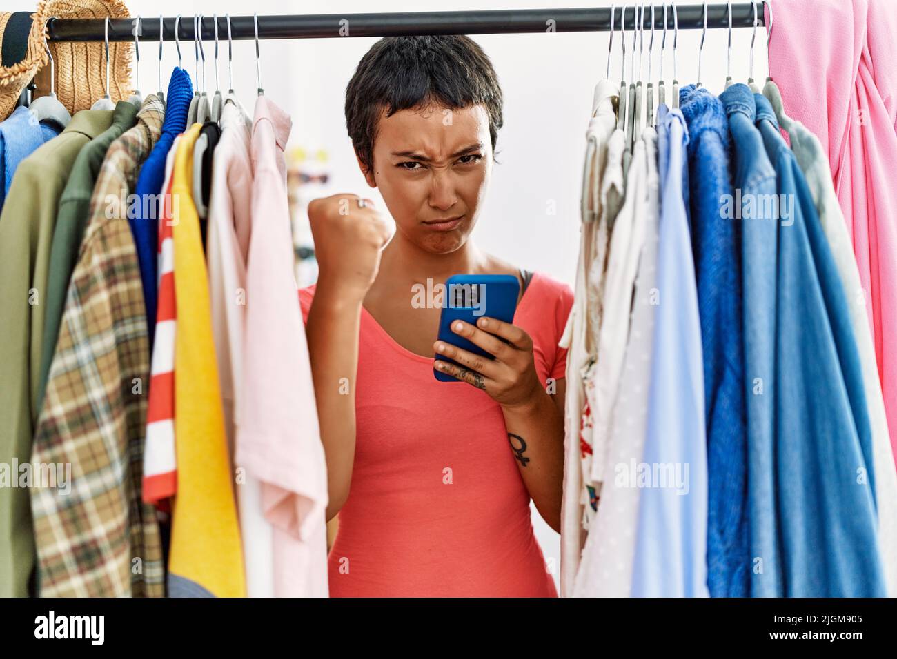 Young hispanic woman with short hair searching clothes on clothing rack ...