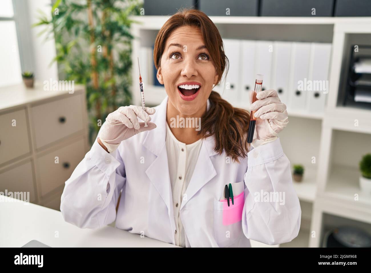 Hispanic doctor woman holding blood sample and syringe angry and mad ...