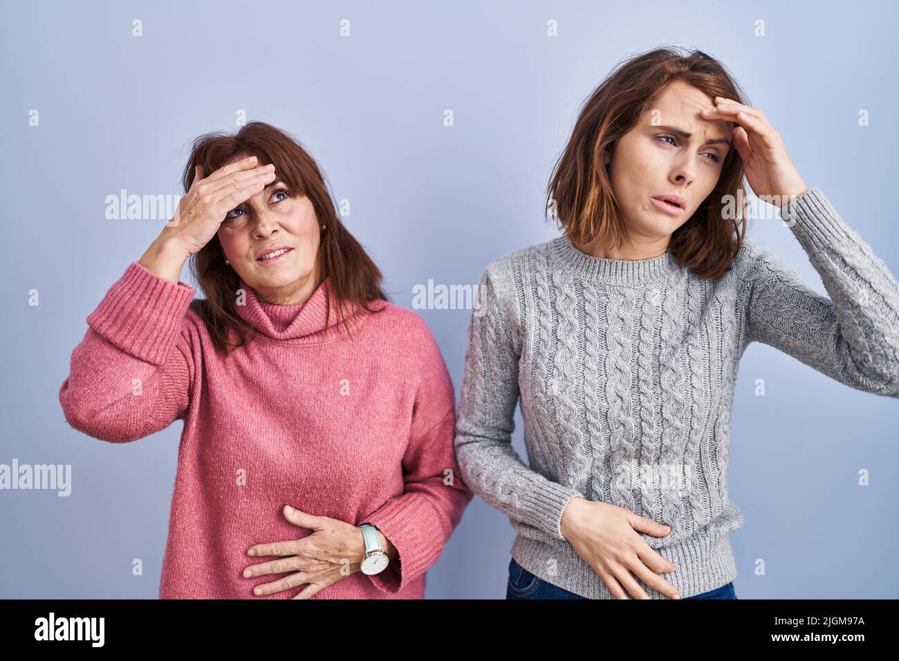 Mother and daughter standing over blue background touching forehead for ...