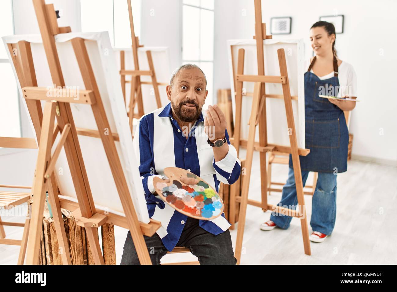 Senior artist man at art studio doing money gesture with hands, asking ...