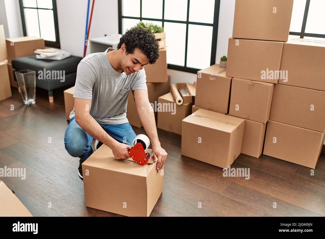 Young hispanic man smiling happy packing box at new home Stock Photo ...
