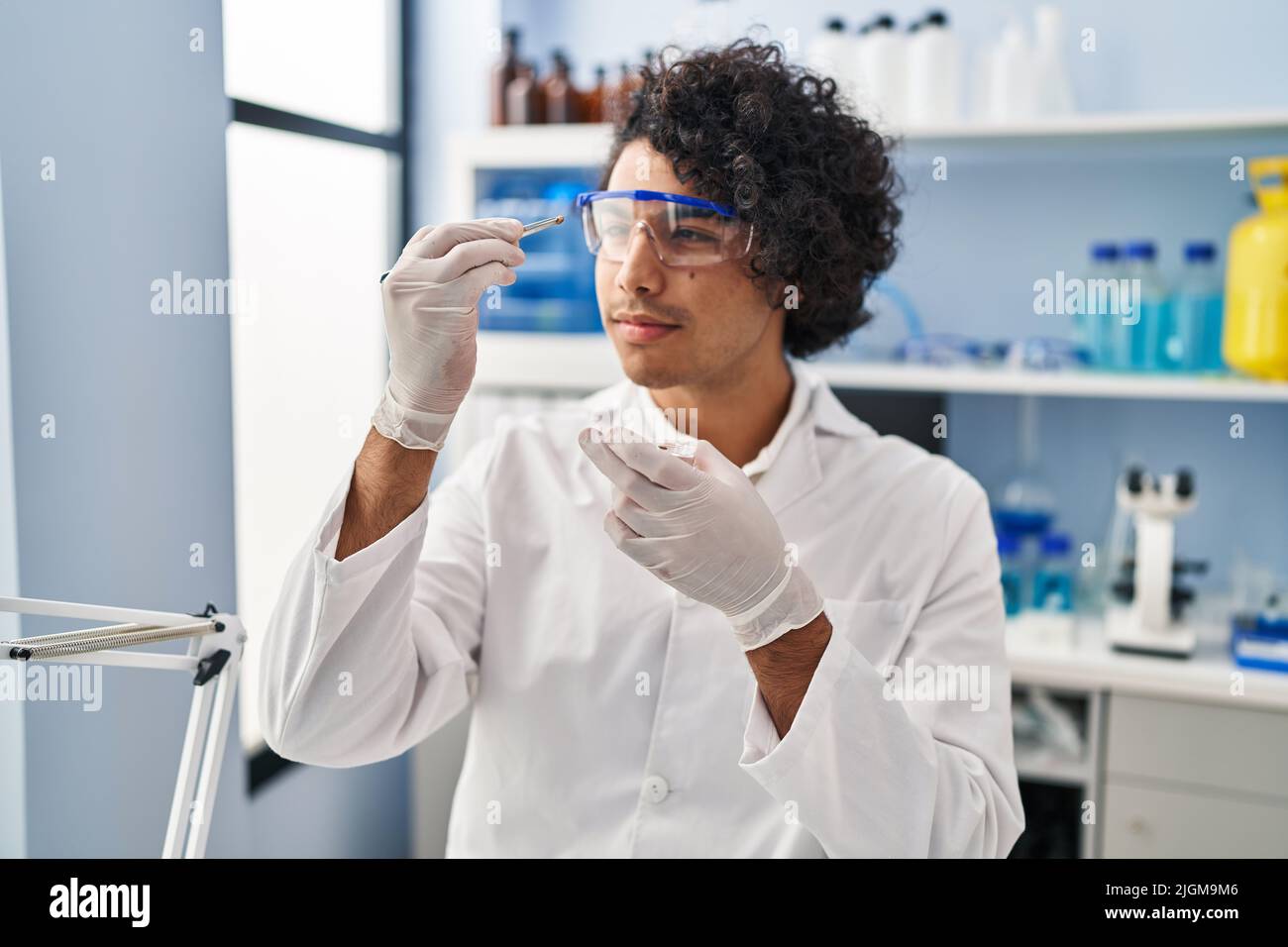Young hispanic man wearing scientist uniform holding sample with ...