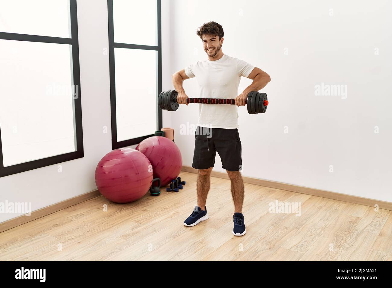Young hispanic man smiling confident training with dumbbell at sport ...