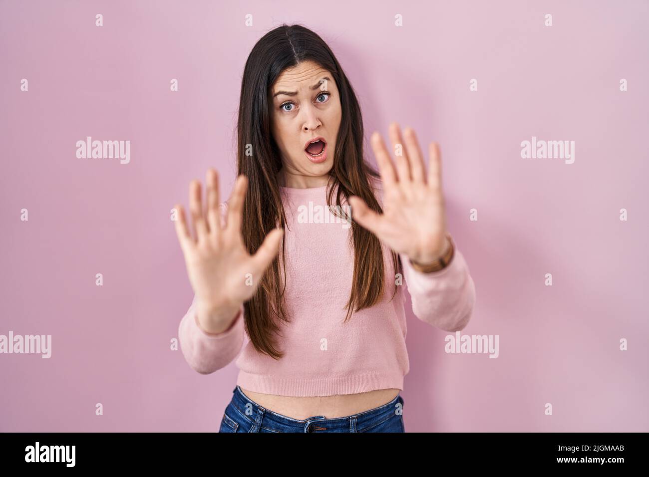 Young brunette woman standing over pink background afraid and terrified ...