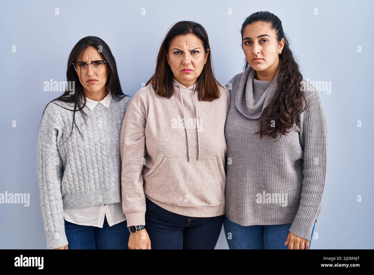 Mother and two daughters standing over blue background skeptic and ...