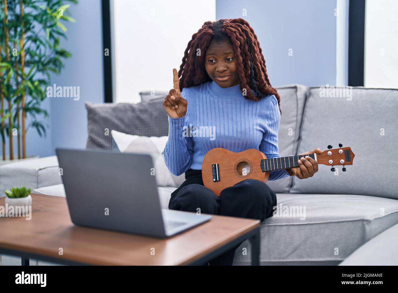 African woman playing ukulele at home doing video call smiling with an ...