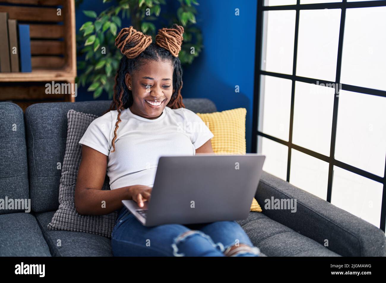 African woman with braided hair using laptop at home with a happy and ...