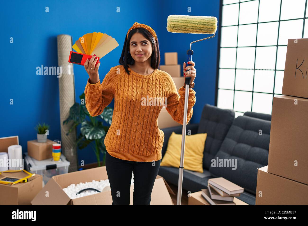 Young hispanic woman painting home walls with paint roller smiling ...