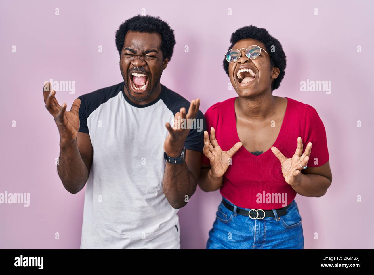 Young african american couple standing over pink background crazy and ...