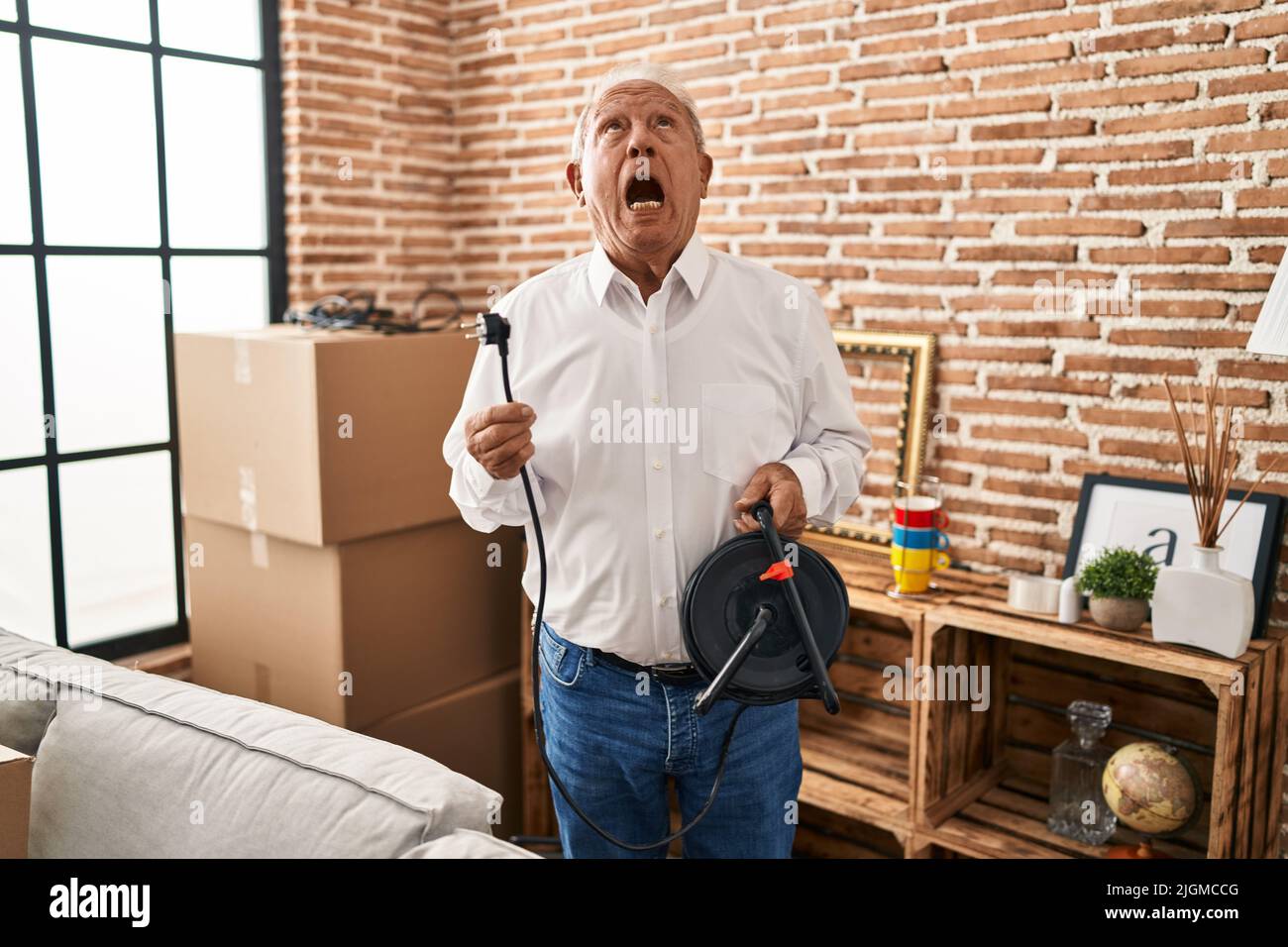 Senior man with grey hair holding extension plug angry and mad ...