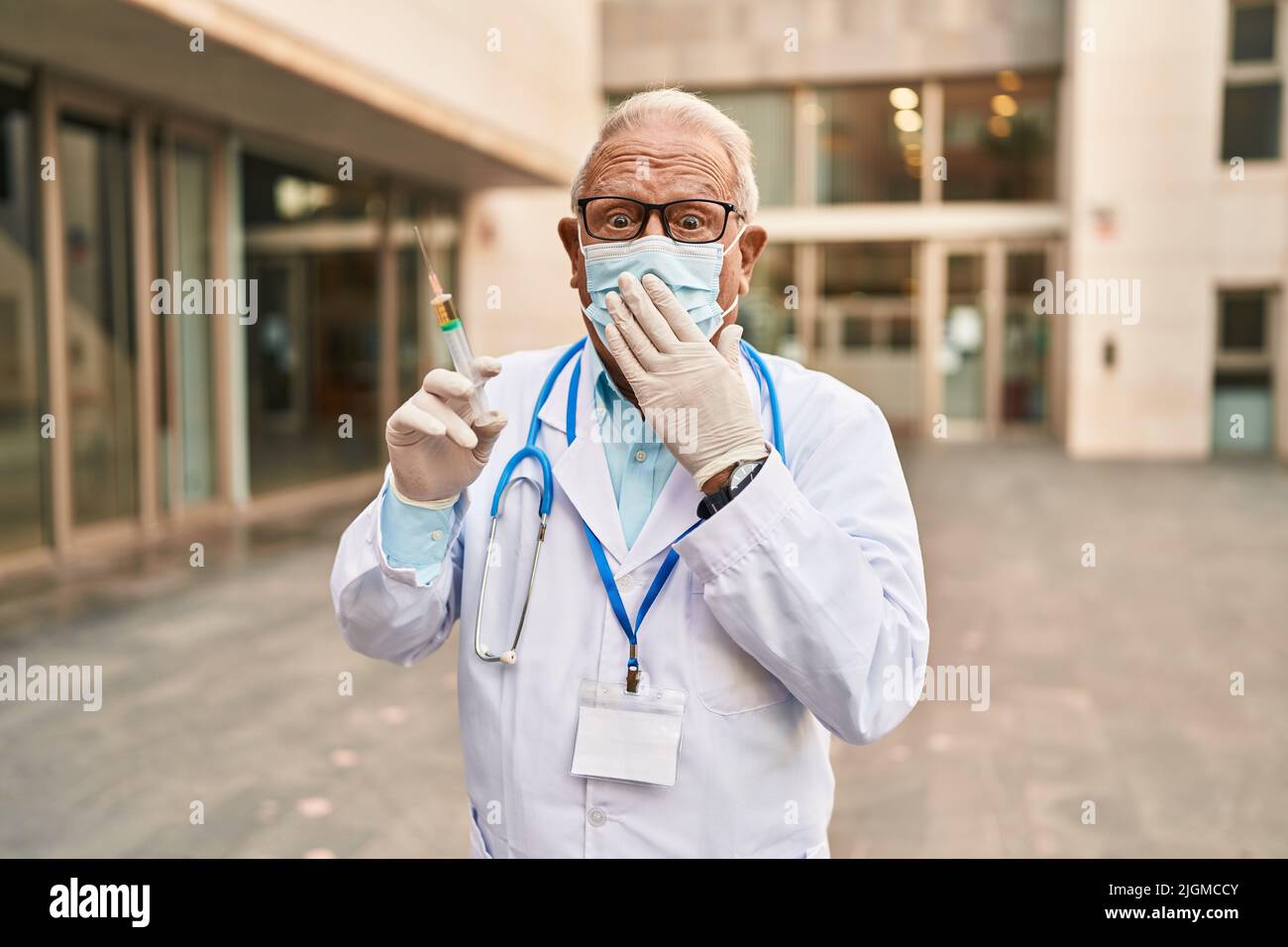 Senior doctor with grey hair wearing safety mask holding syringe ...