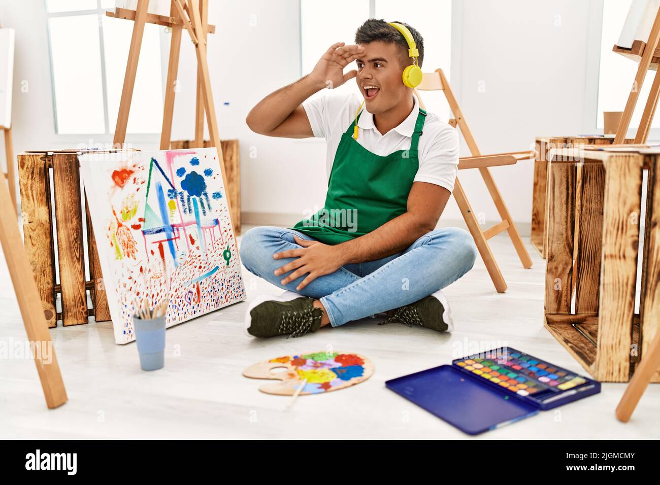 Young hispanic man at art studio very happy and smiling looking far ...