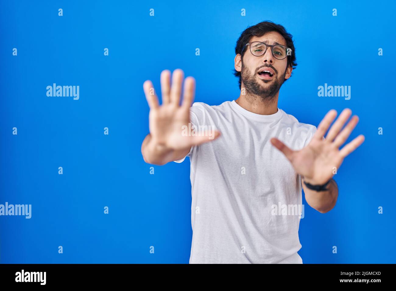 Handsome latin man standing over blue background afraid and terrified ...