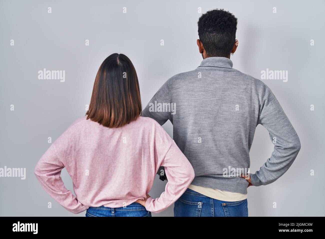 Young hispanic couple standing together standing backwards looking away ...