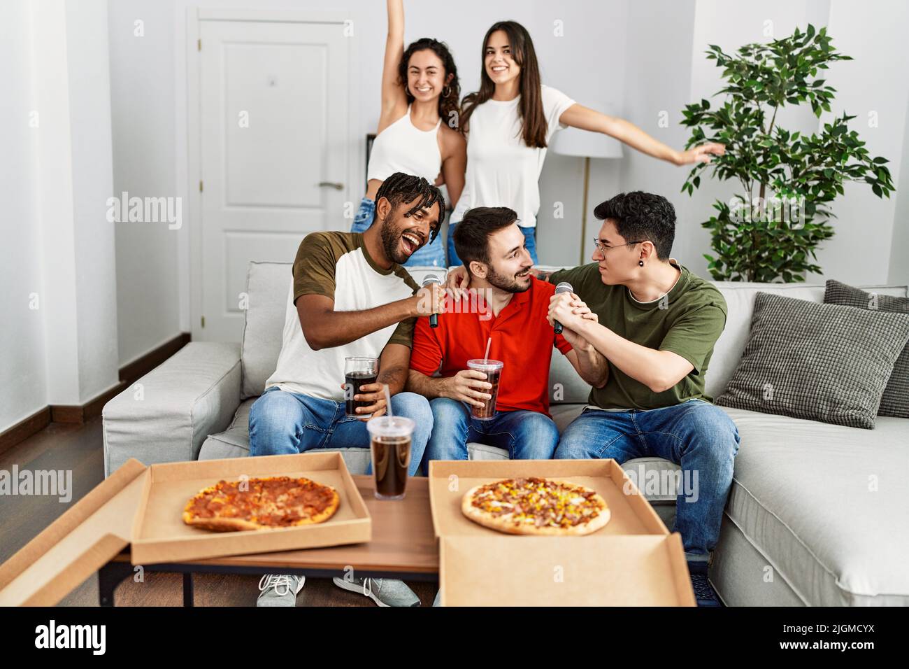 Group of young friends having party eating italian pizza and singing ...
