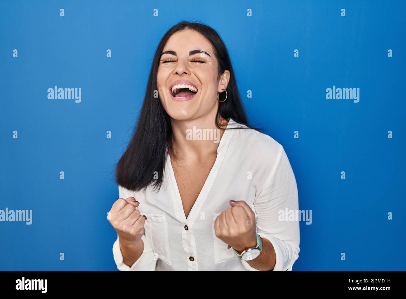 Young hispanic woman standing over blue background very happy and ...