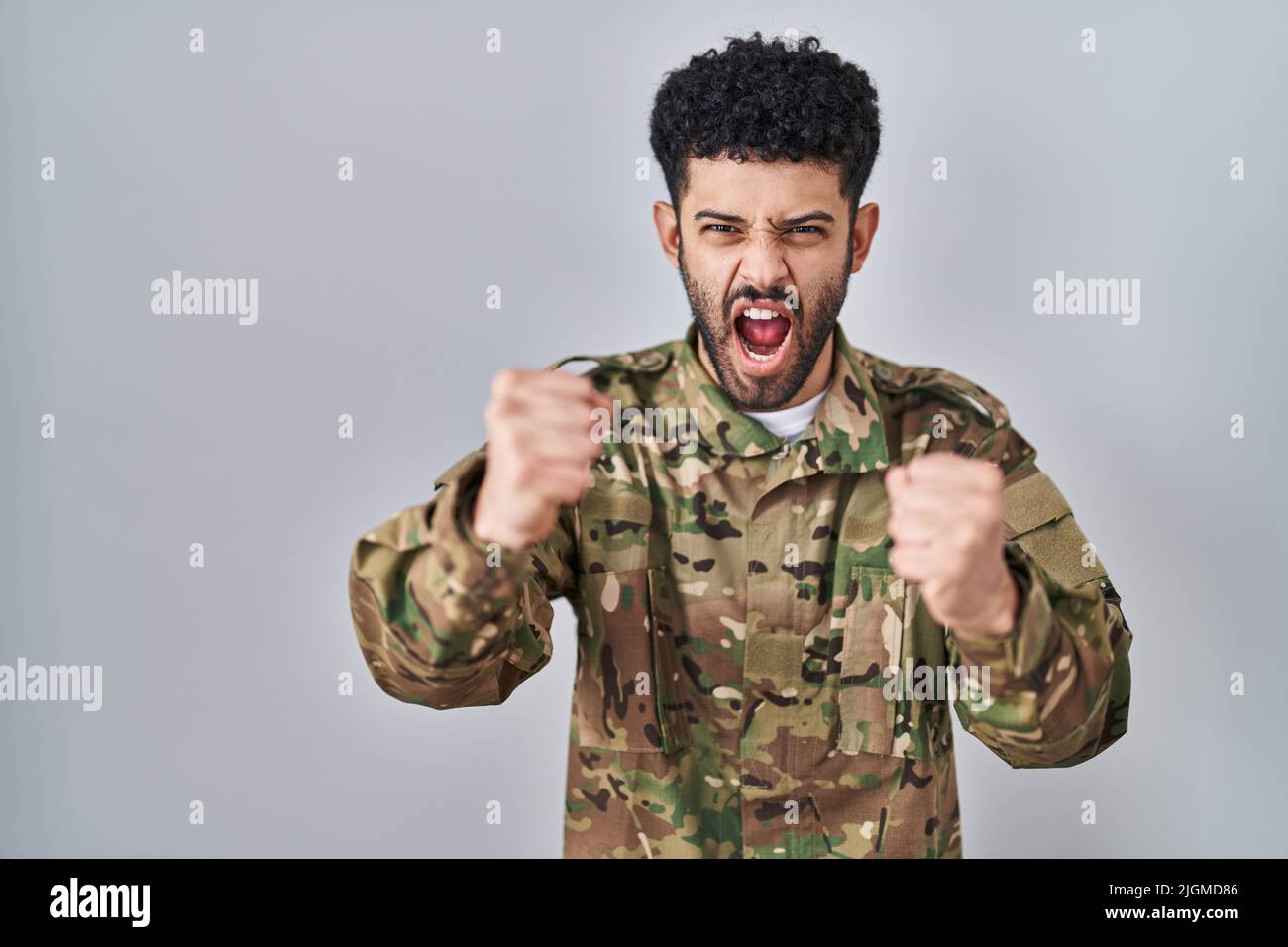 Arab man wearing camouflage army uniform angry and mad raising fists ...