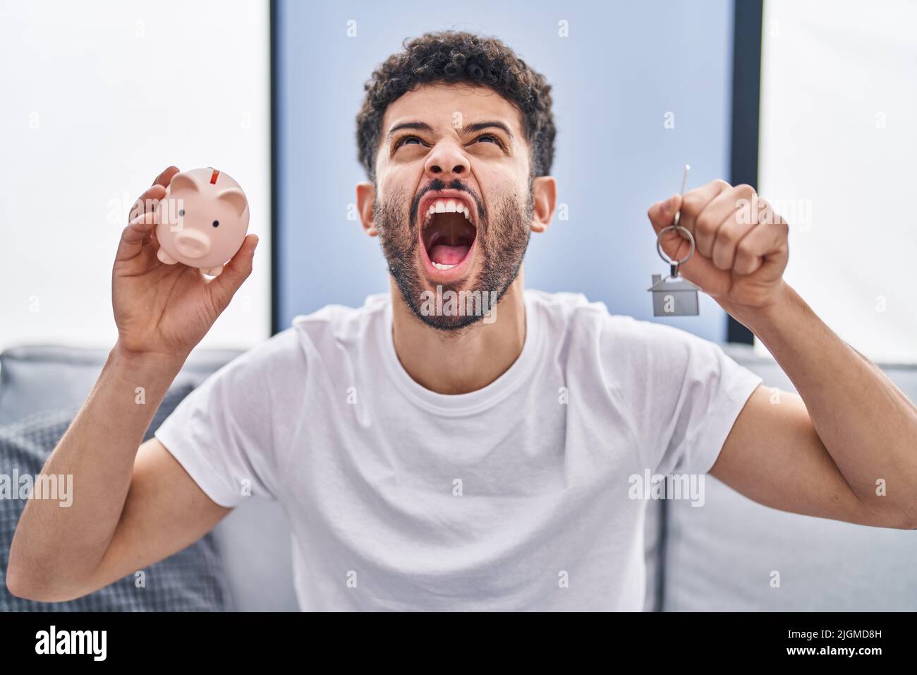 Arab man holding piggy bank and house keys angry and mad screaming ...