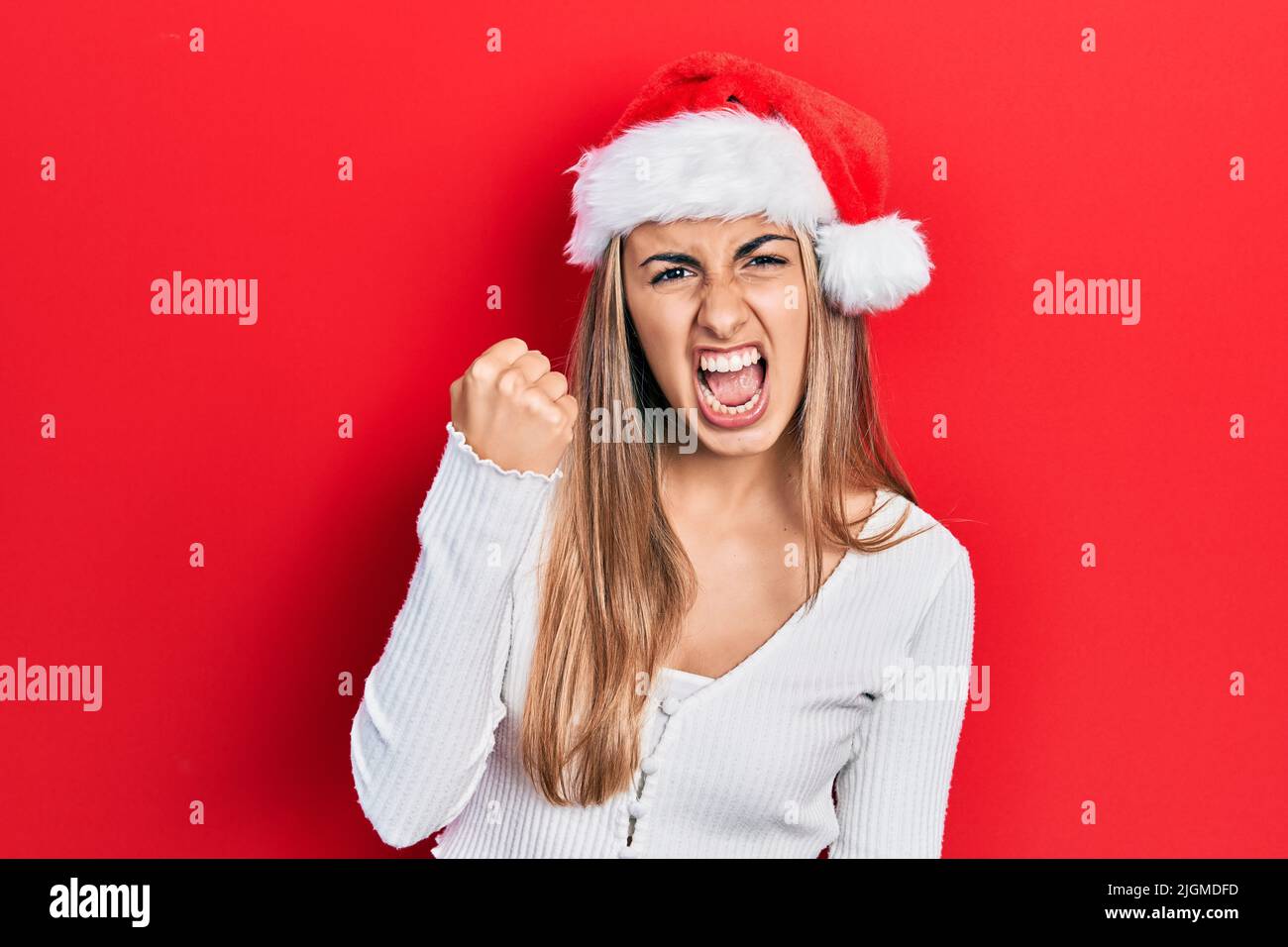 Beautiful hispanic woman wearing christmas hat angry and mad raising ...