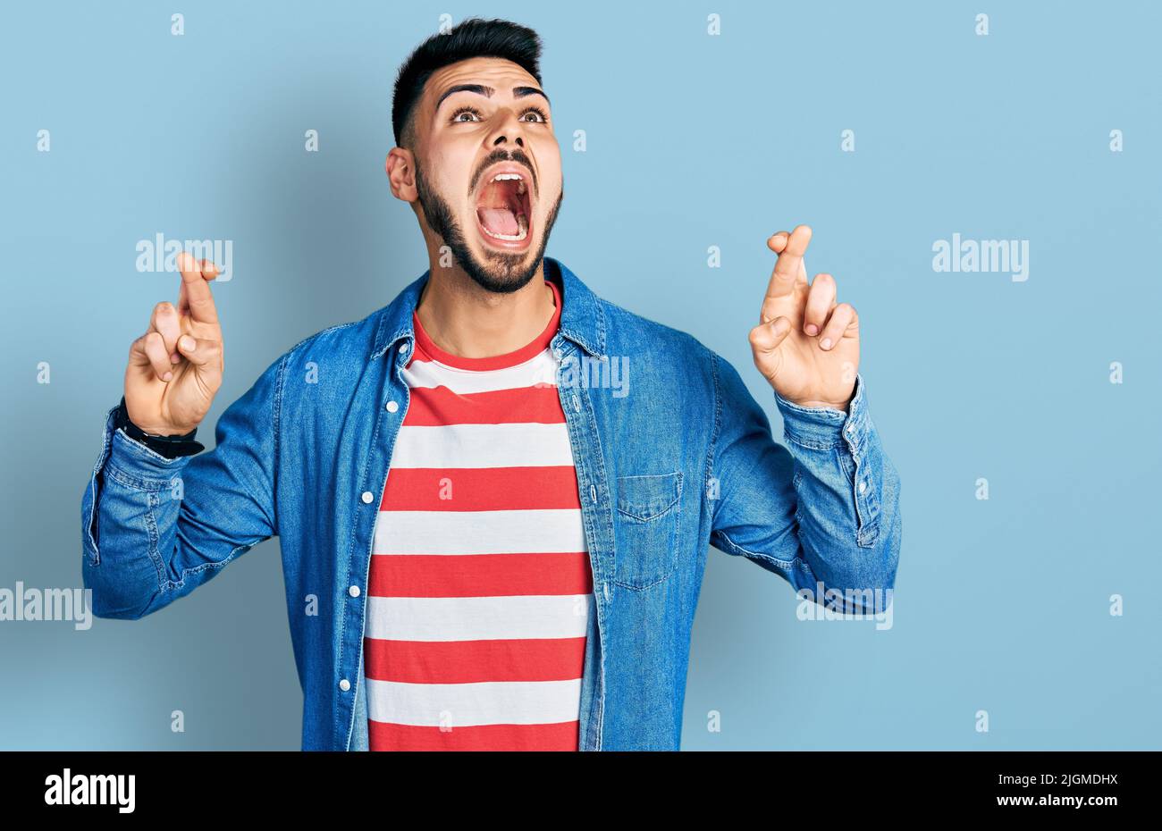 Young hispanic man with beard doing fingers crossed luck gesture angry ...