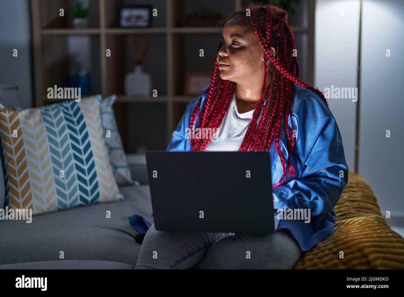 African american woman with braided hair using computer laptop at night ...