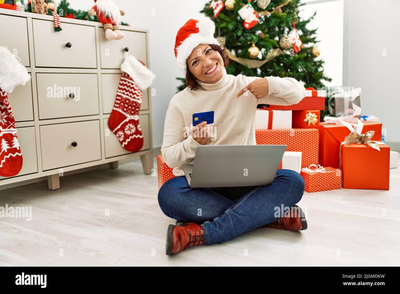 Middle age hispanic woman wearing christmas hat holding gift and credit ...