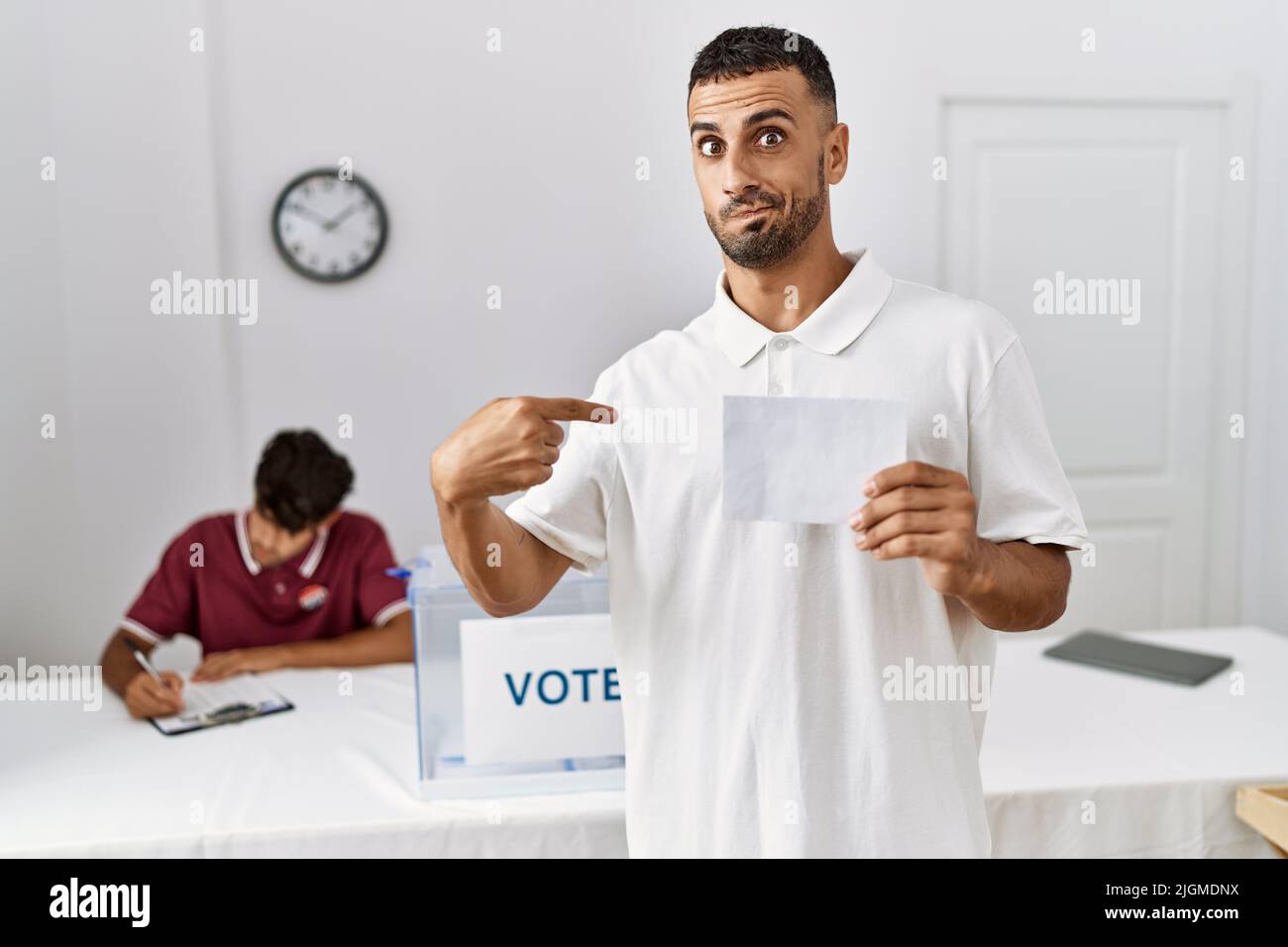 Young hispanic man voting putting envelop in ballot box pointing finger ...