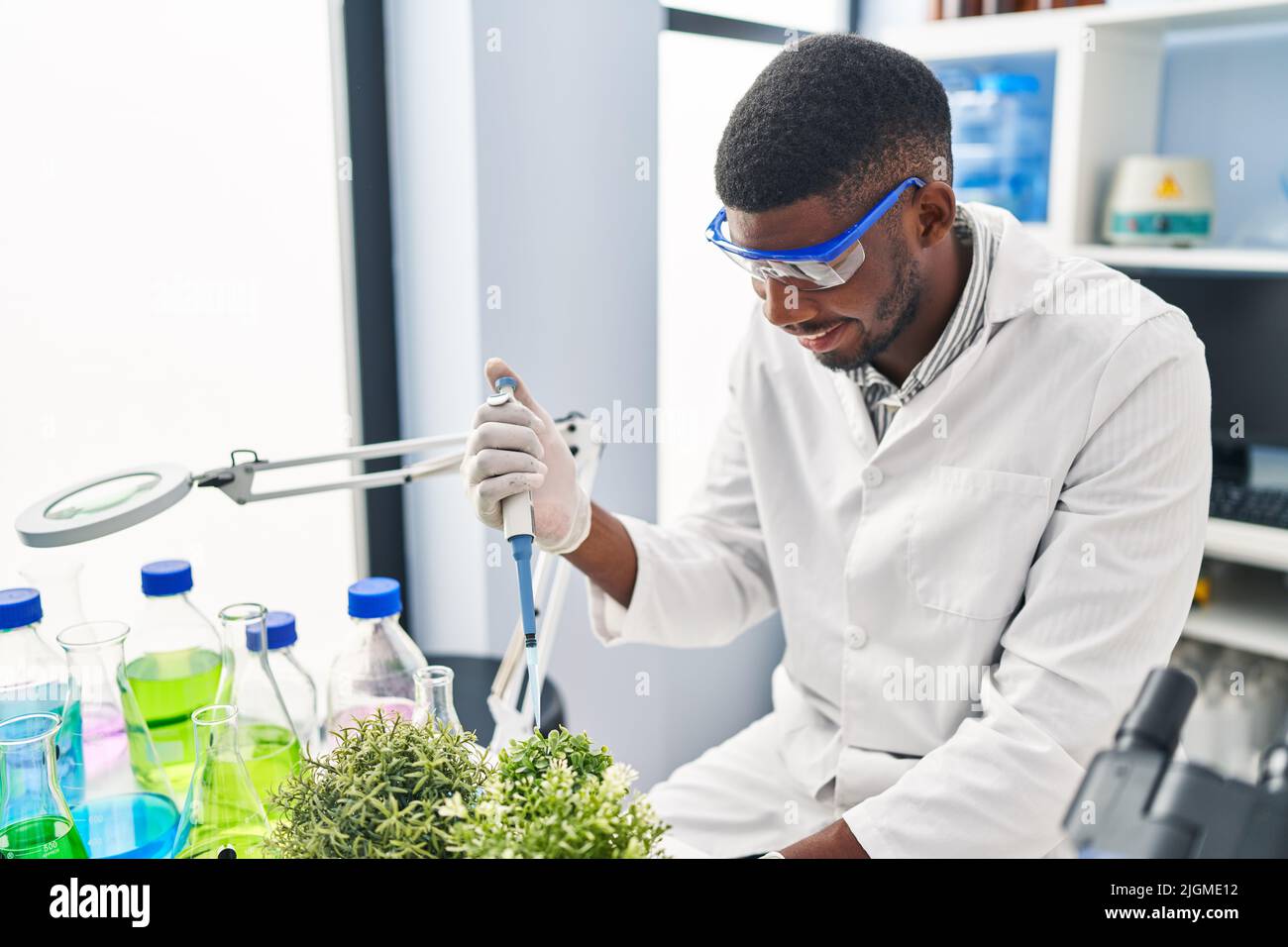 Young african american man wearing scientist uniform using pipette on ...