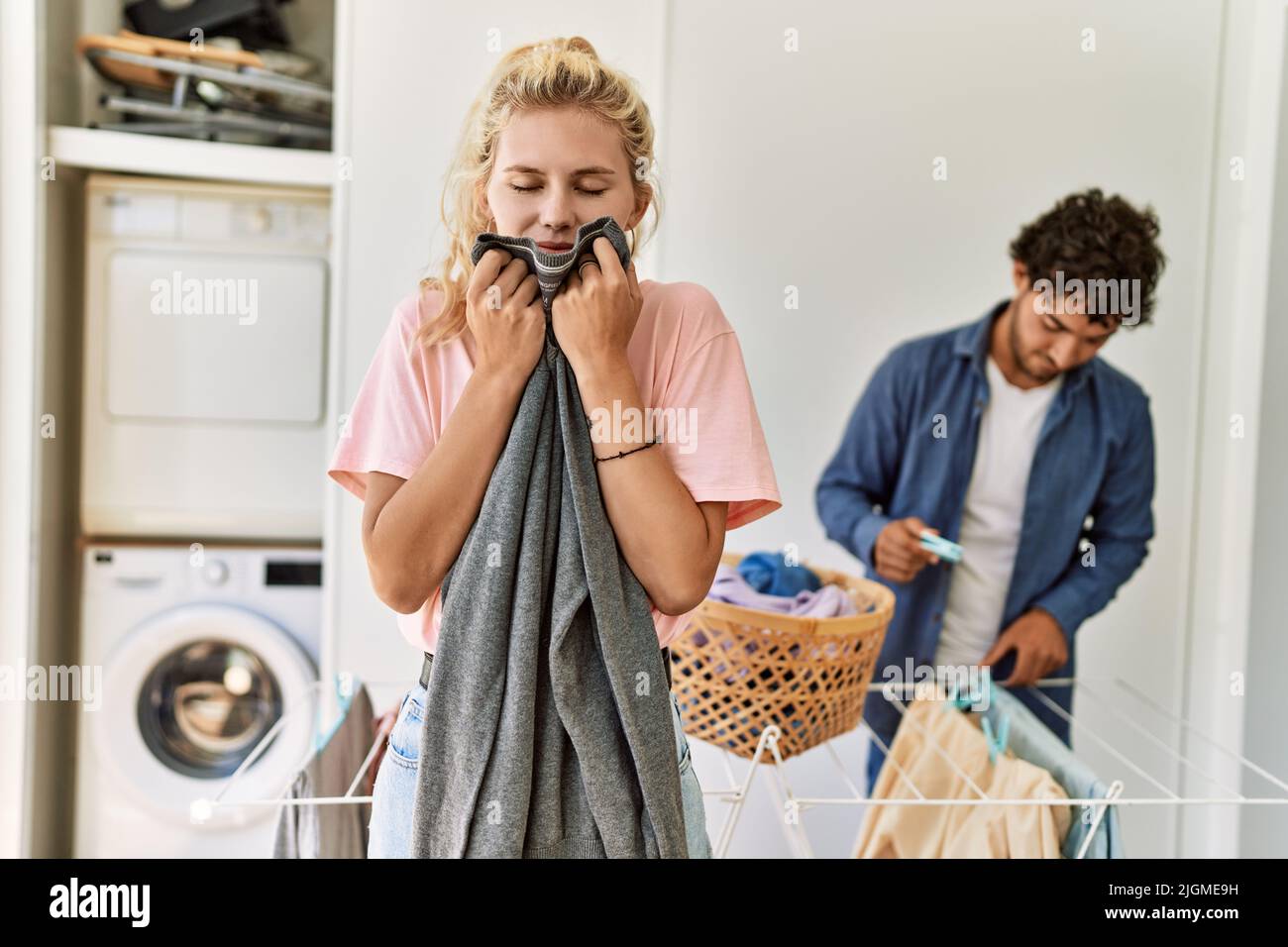 Young couple smiling happy doing laundry. Woman smelling clean clothes ...