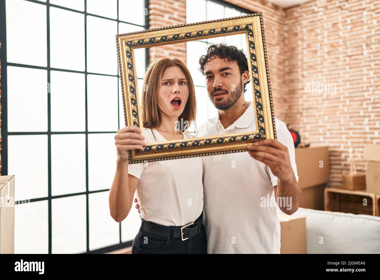 Young two people holding empty frame together in shock face, looking ...