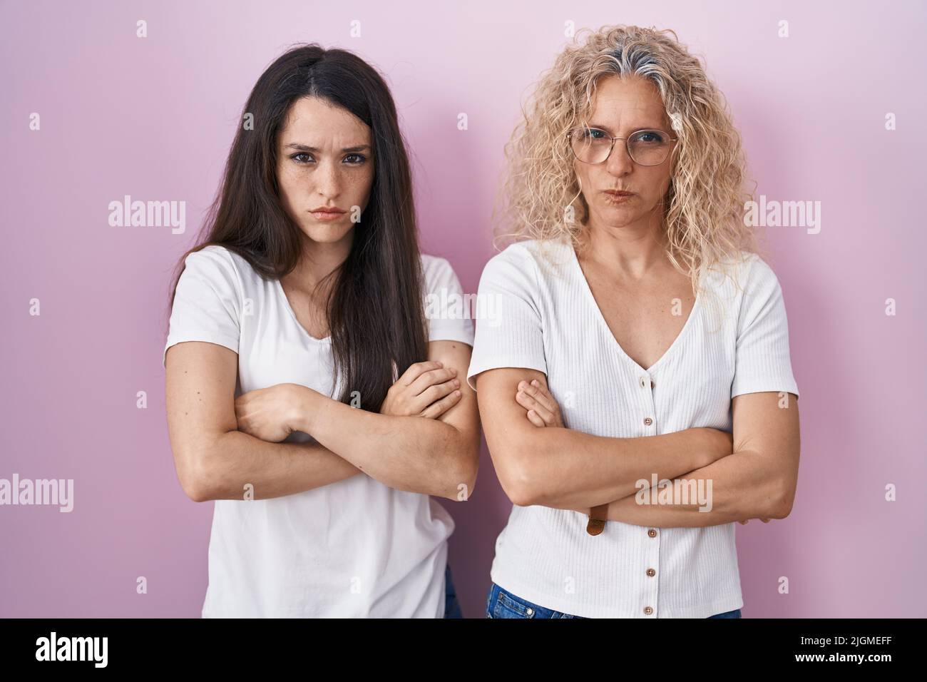 Mother And Daughter Standing Together Over Pink Background Skeptic And