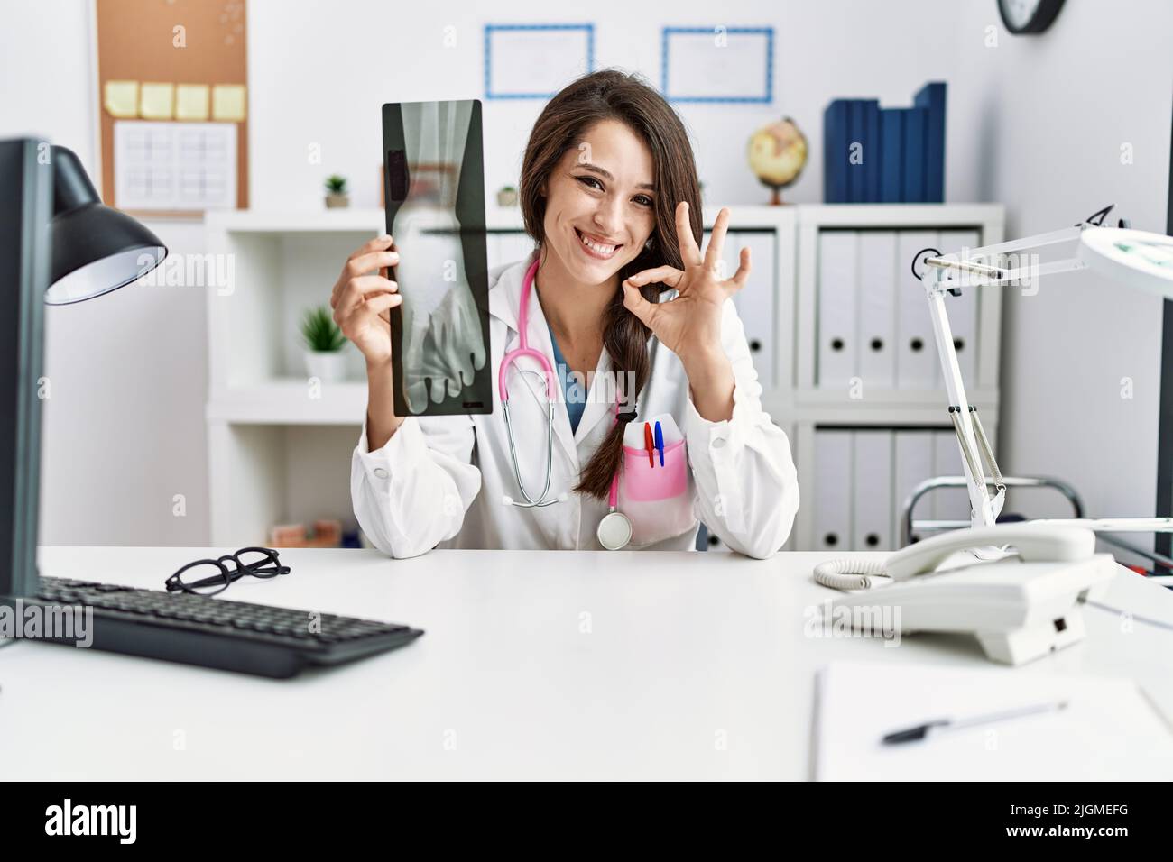 Young doctor woman holding foot x-ray doing ok sign with fingers ...